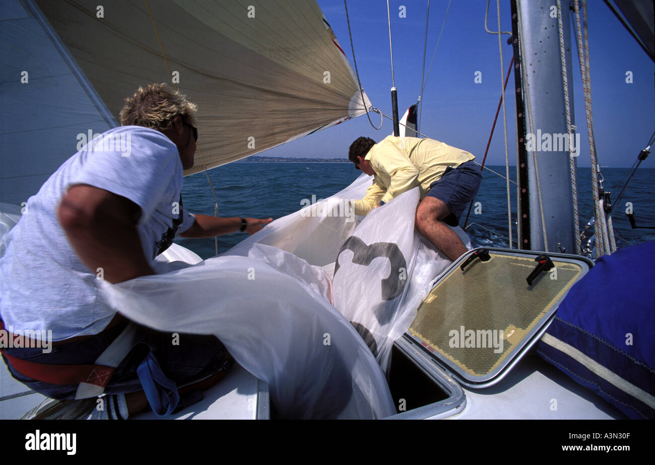 Two crew members take down a spinnaker and store it below ready for the ...