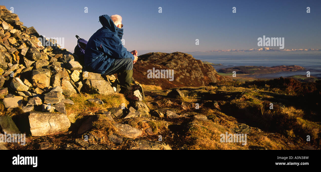 Hill walker sitting on cairn on Screel Hill looking across the Solway ...