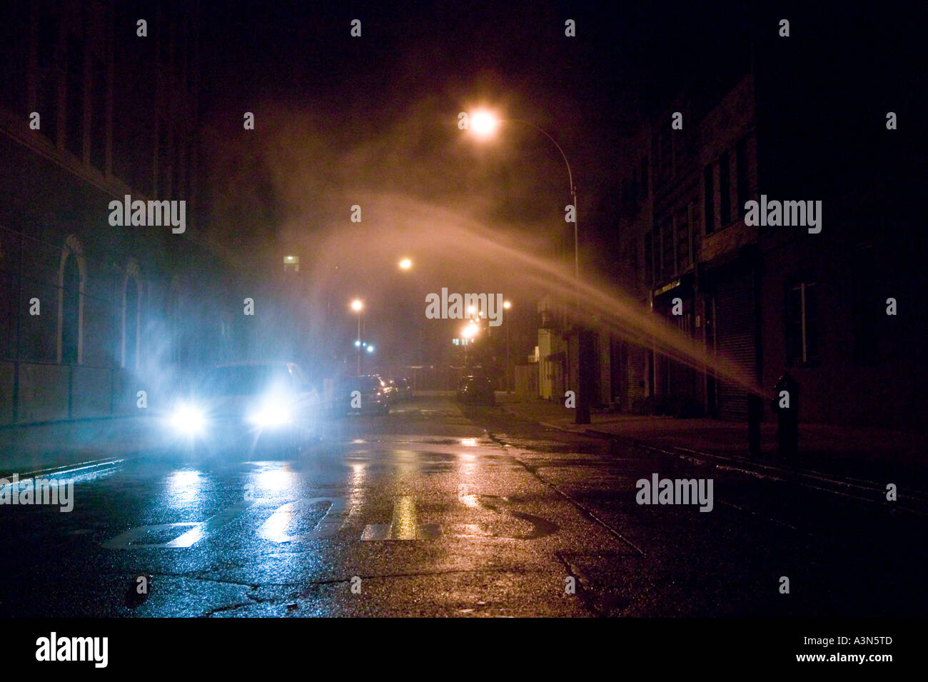 A car passes under the spray of an open fire hydrant in a street of ...
