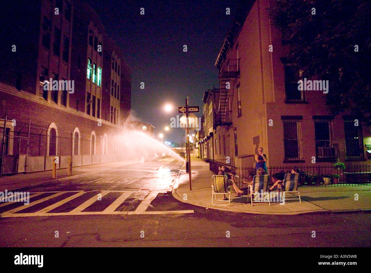 a family relaxes on deck chairs near an open fire hydrant on a street ...