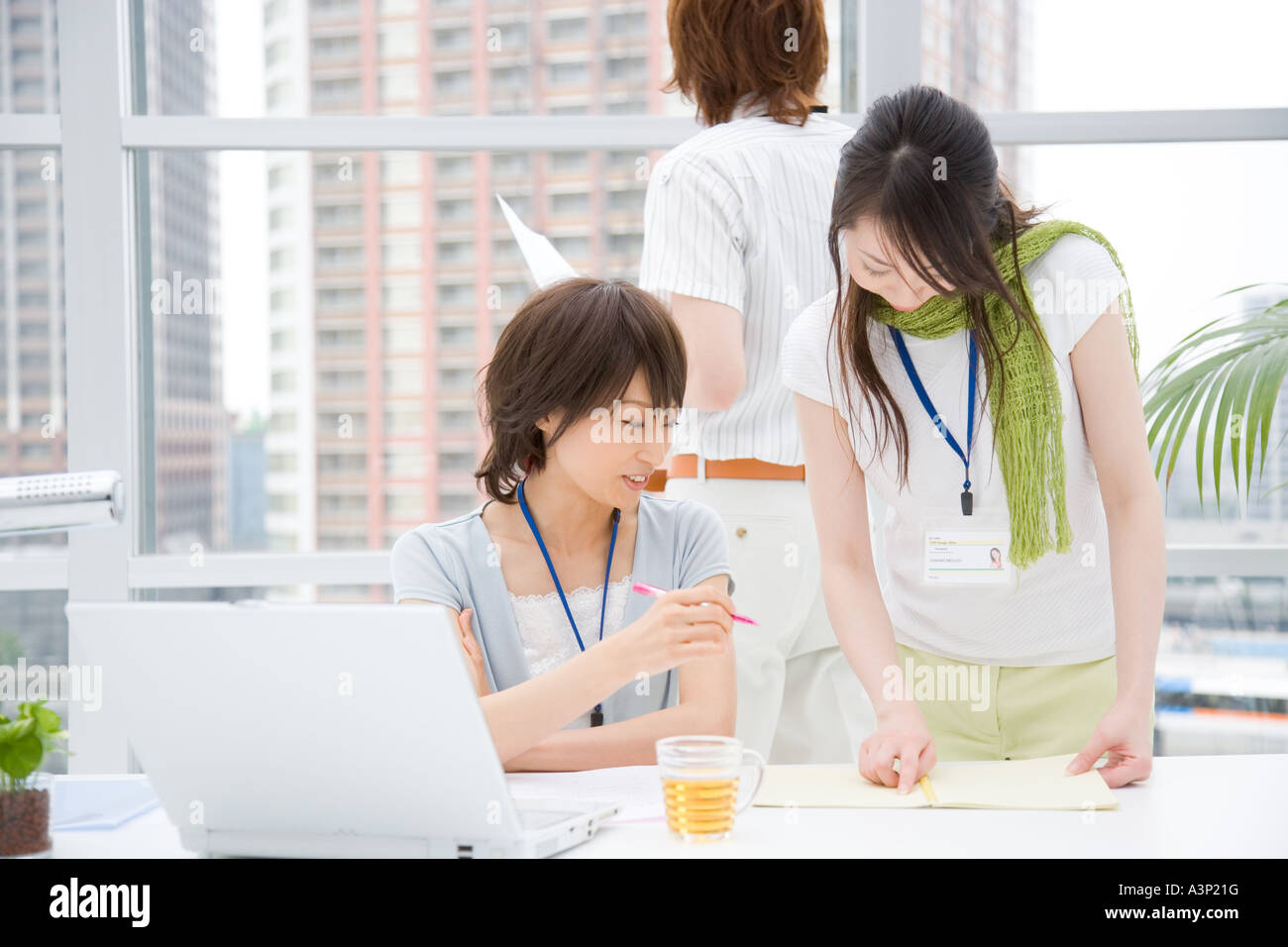 Two young women looking at notebook and young man standing behind Stock ...