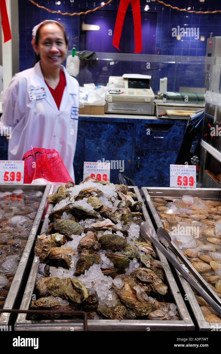 Friendly seafood market worker with trays of fresh oysters and clams on ...
