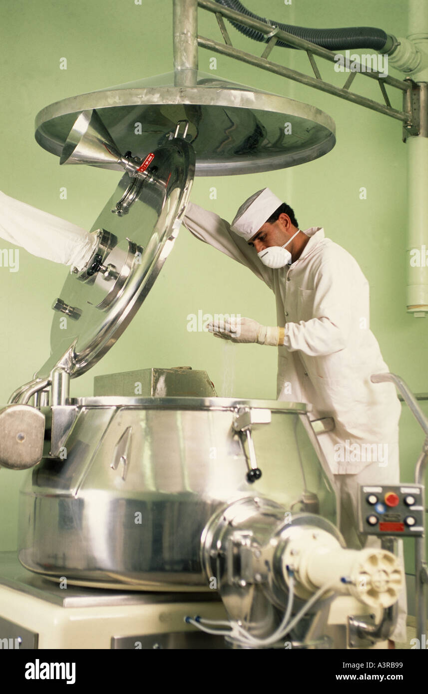 Worker inspecting powder in vat at pharamaceutical manufacturing plant ...