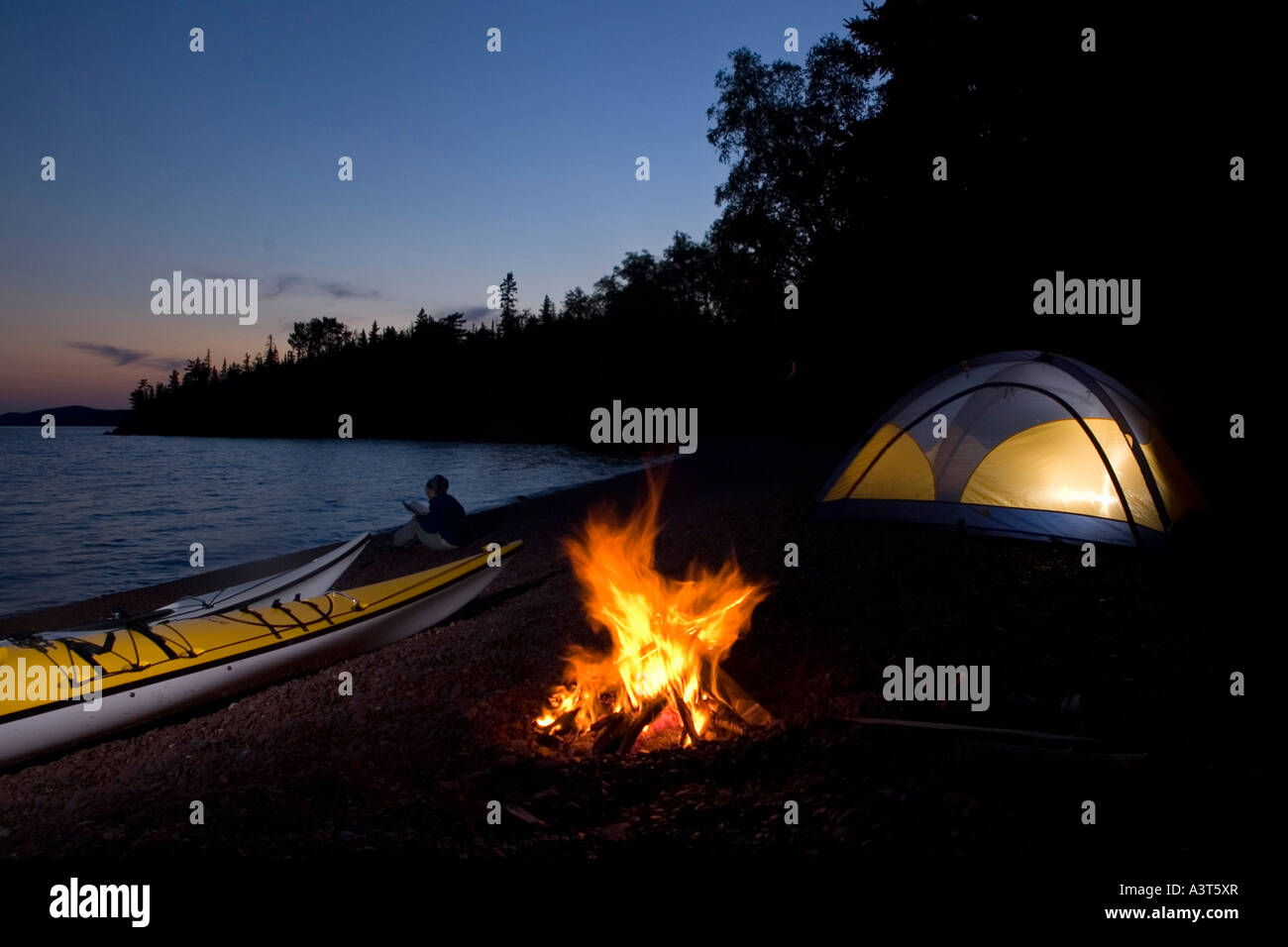 A campfire burns and a tent is lit at a sea kayaker campsite at Fish ...