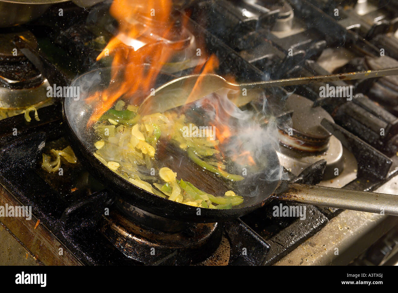 Close up of chef cooking in industrial kitchen adding spice and flames ...