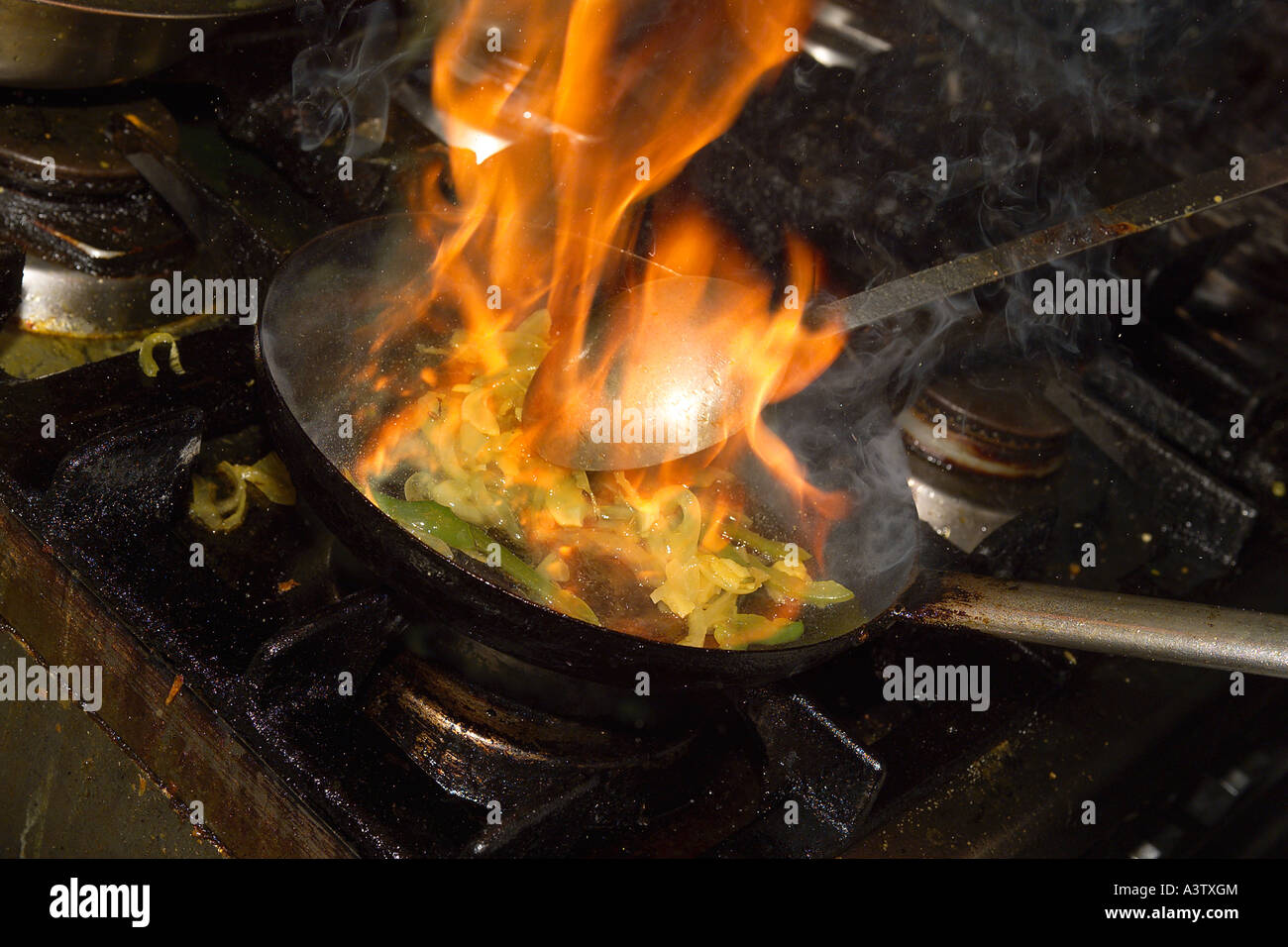 Close up of chef cooking in industrial kitchen adding spice and flames ...
