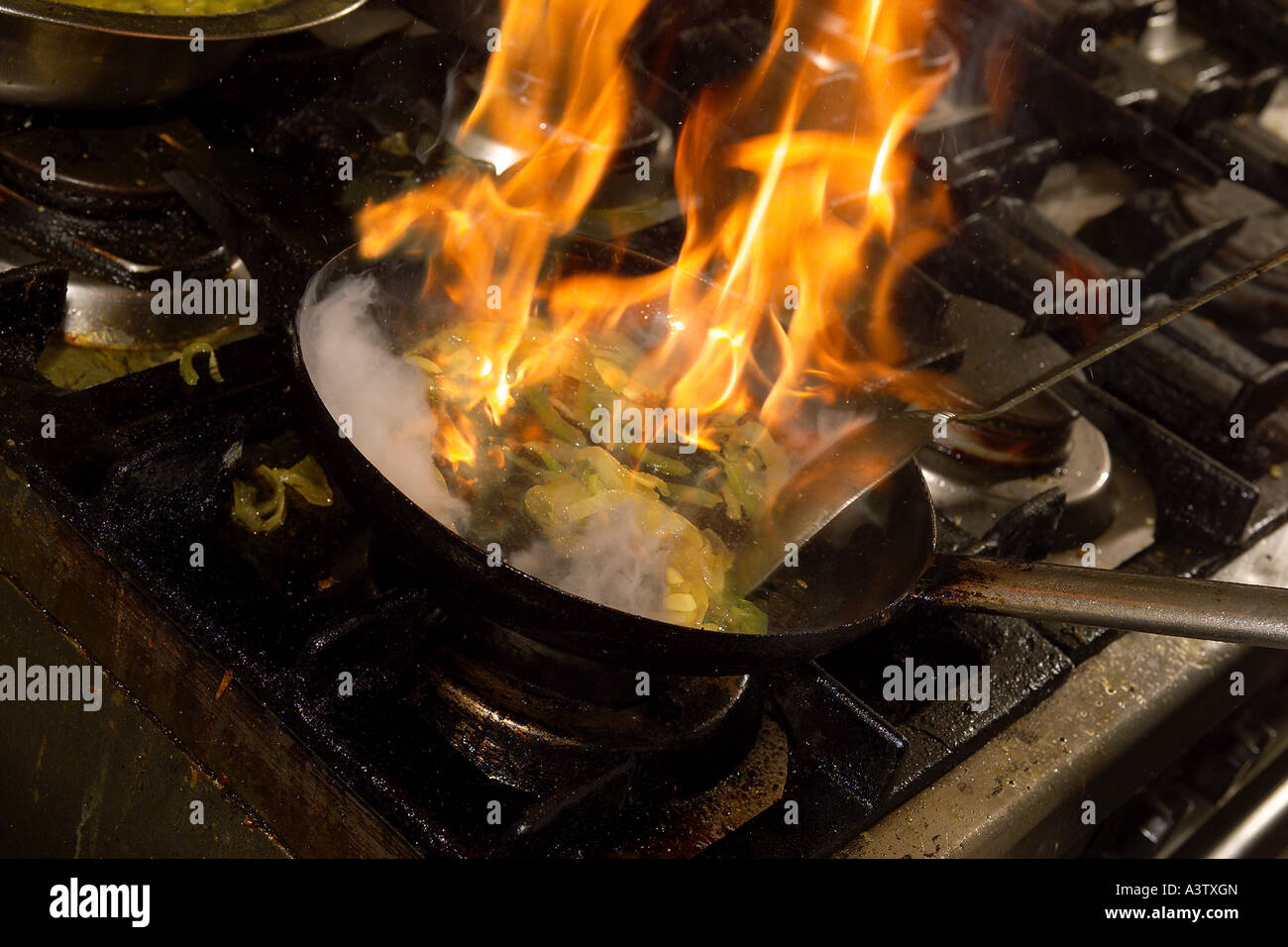 Close up of chef cooking in industrial kitchen adding spice and flames ...