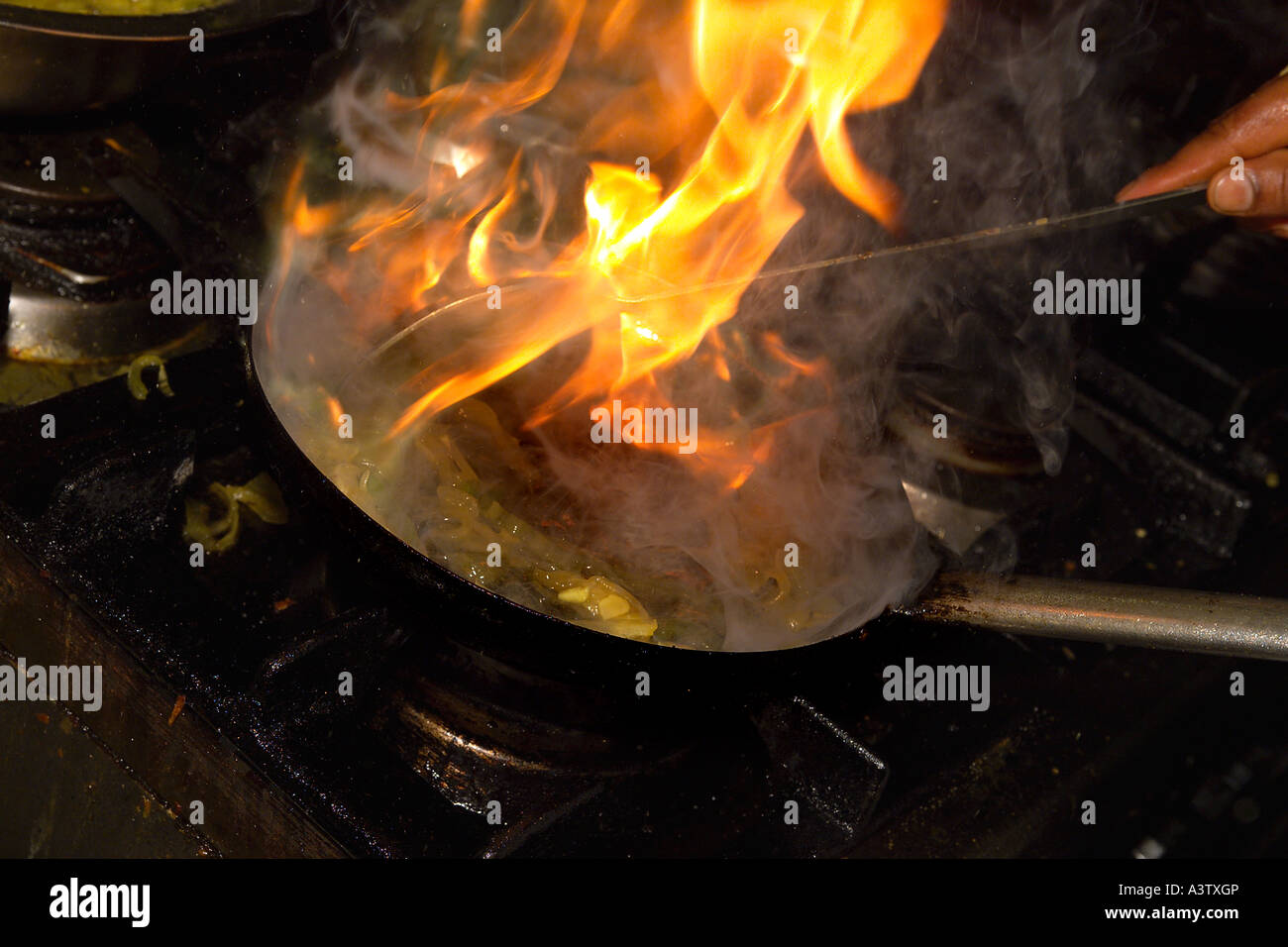 Close up of chef cooking in industrial kitchen adding spice and flames ...