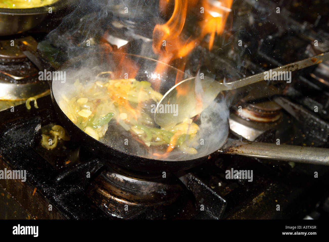 Close up of chef cooking in industrial kitchen adding spice and flames ...