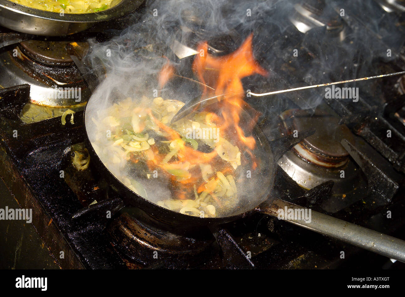 Close up of chef cooking in industrial kitchen adding spice and flames ...
