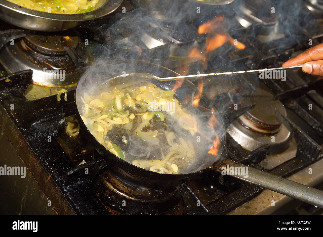 Close up of chef cooking in industrial kitchen adding spice and flames ...