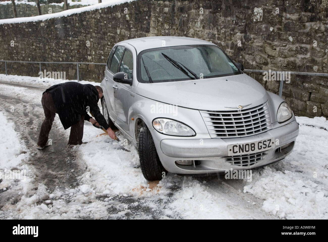 Motorist digging out car stuck in snow and adding salt under tyres ...