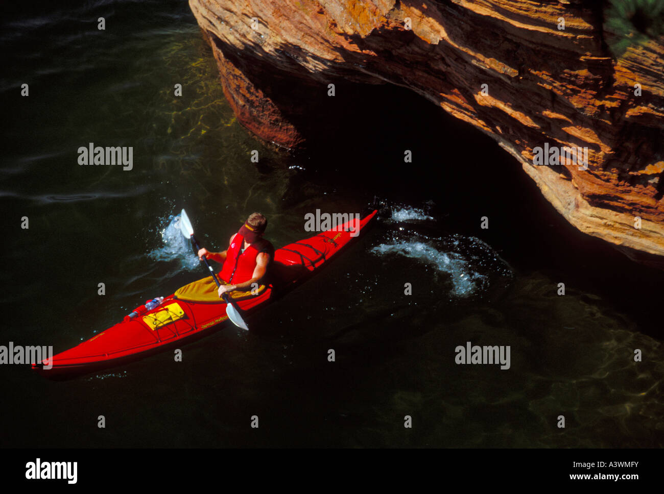 A KAYAKER EXITS A SEA CAVE AT SQUAW POINT IN THE APOSTLE ISLANDS ...