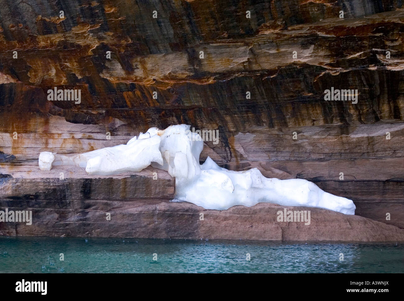 Ice clings to the base of colored sandstone cliffs in Pictured Rocks ...