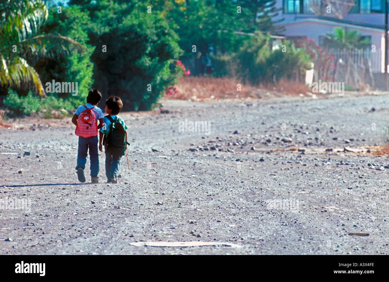 Two small boys with backpacks walk unmade rocky road Baja California ...