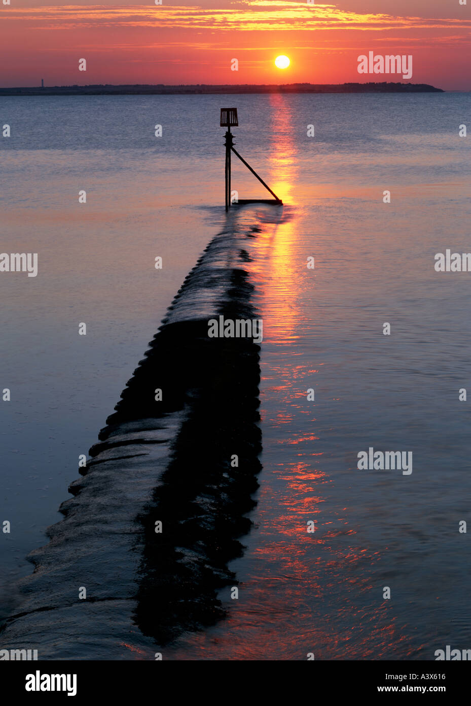 sun setting above a break water and the isle of sheppey from Whitstable ...