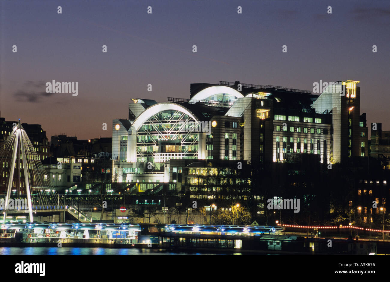 charing cross station building at night lit up with the river thames in ...