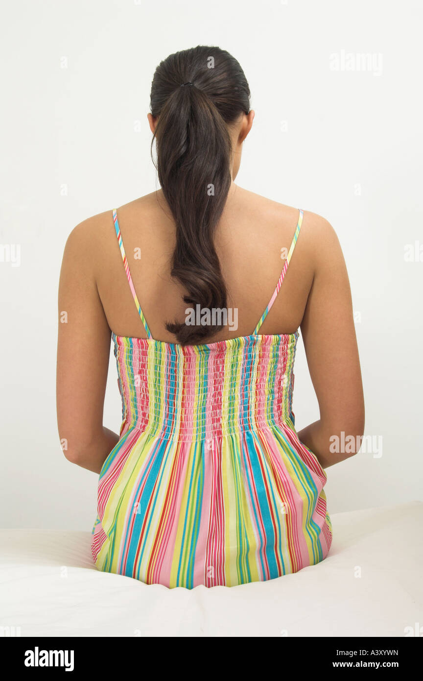 rear view of young woman with ponytail sitting on bed in colourful ...