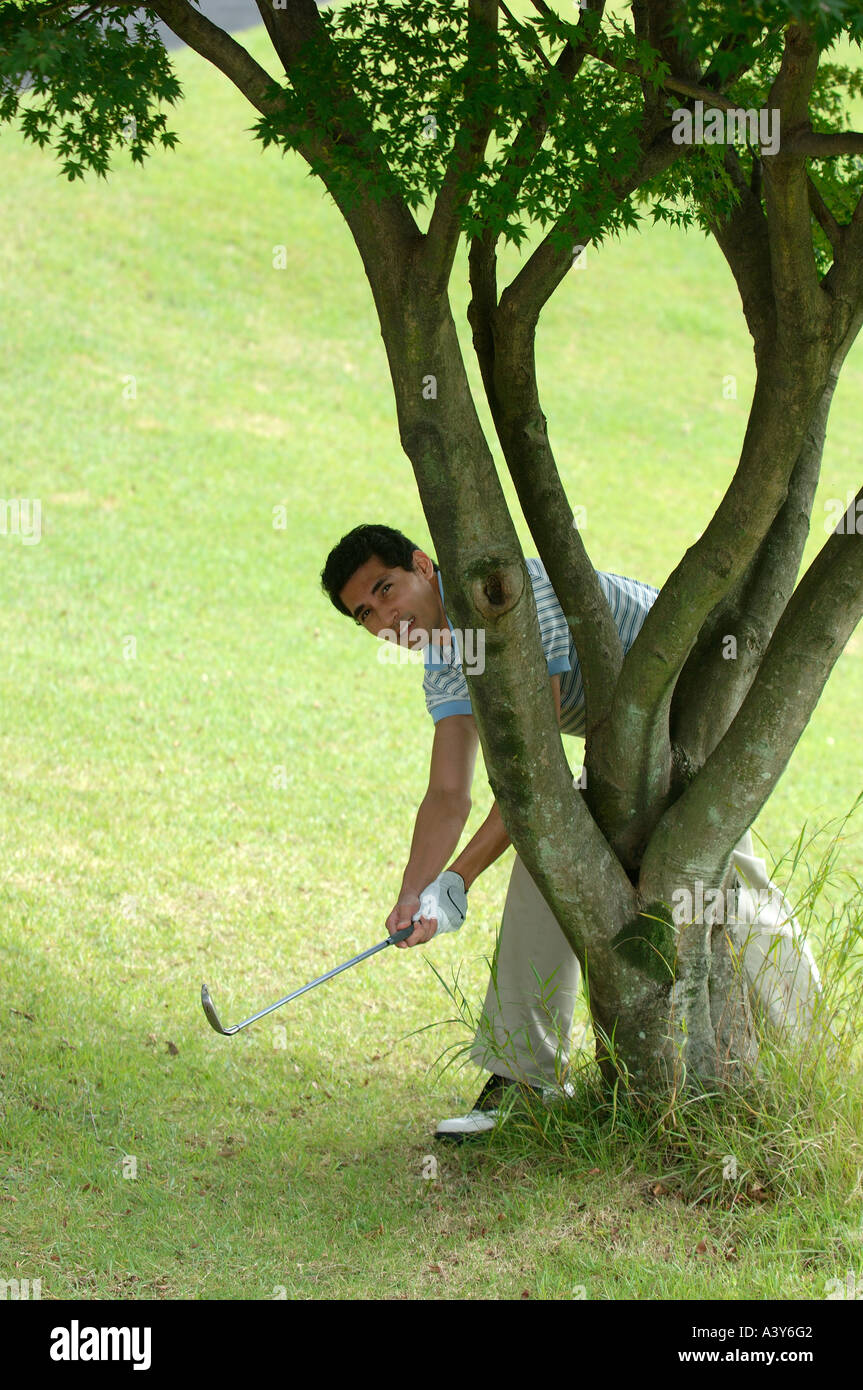 Man playing a golf shot from behind a tree Stock Photo - Alamy