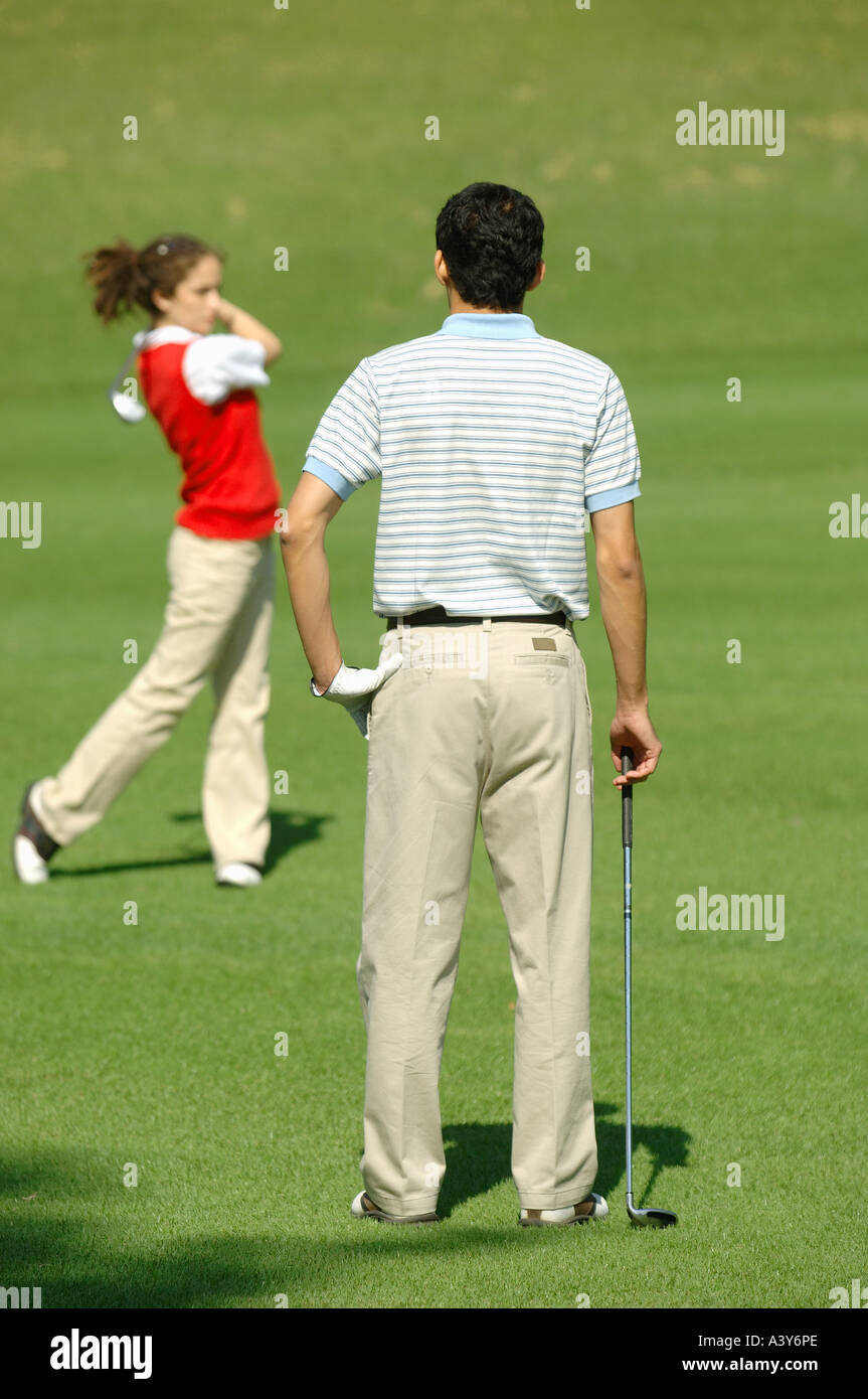 Man watching a woman play a golf shot Stock Photo - Alamy