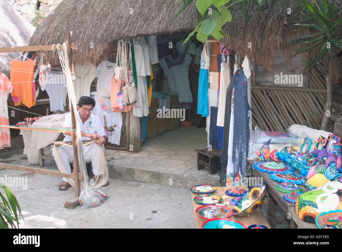 Mayan male artist working beside art display in front of wooden hut ...