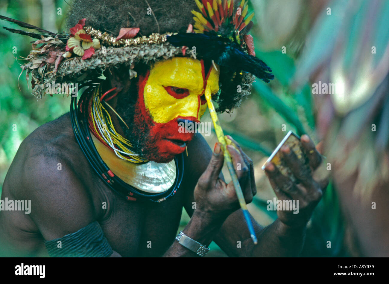 A Huli wigman using a hand mirror to put on traditional face paint Tari ...