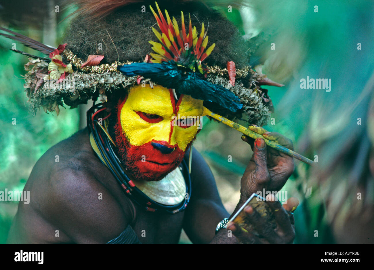 A Huli wigman using a hand mirror to put on traditional face paint Tari ...
