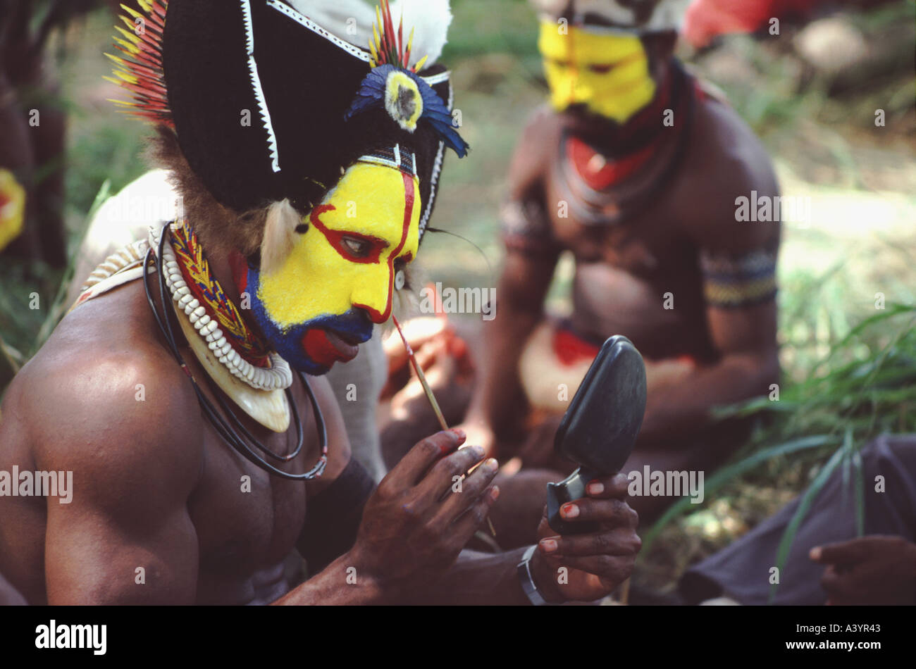 A Huli wigman using a rear view mirror to put on traditional face paint ...