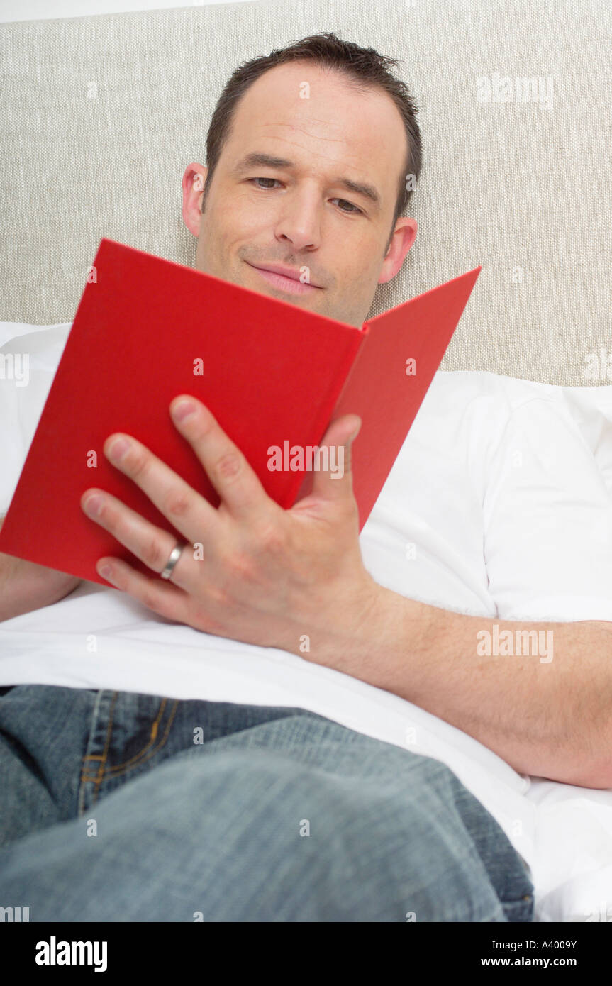 portrait of man lying on bed reading book Stock Photo - Alamy