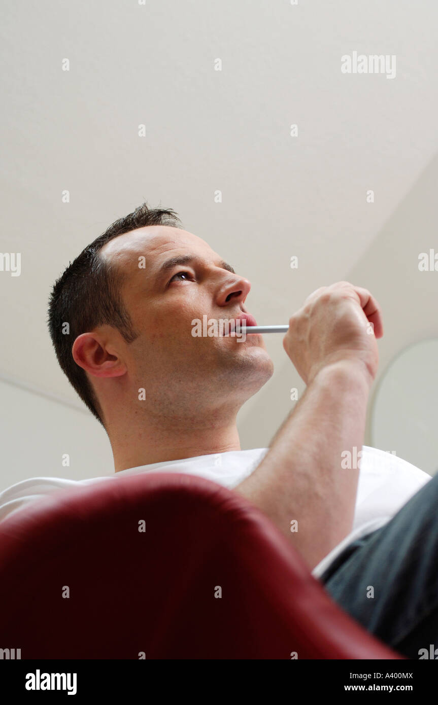 low angle portrait of young man with pen in mouth thinking Stock Photo ...