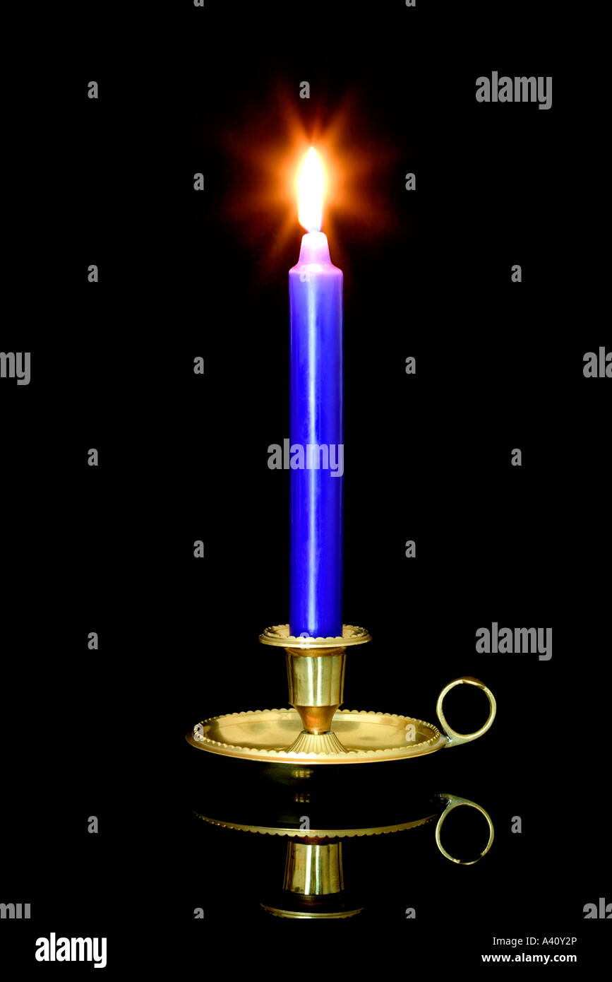 Blue candle and flame in a brass candle holder on a black background ...