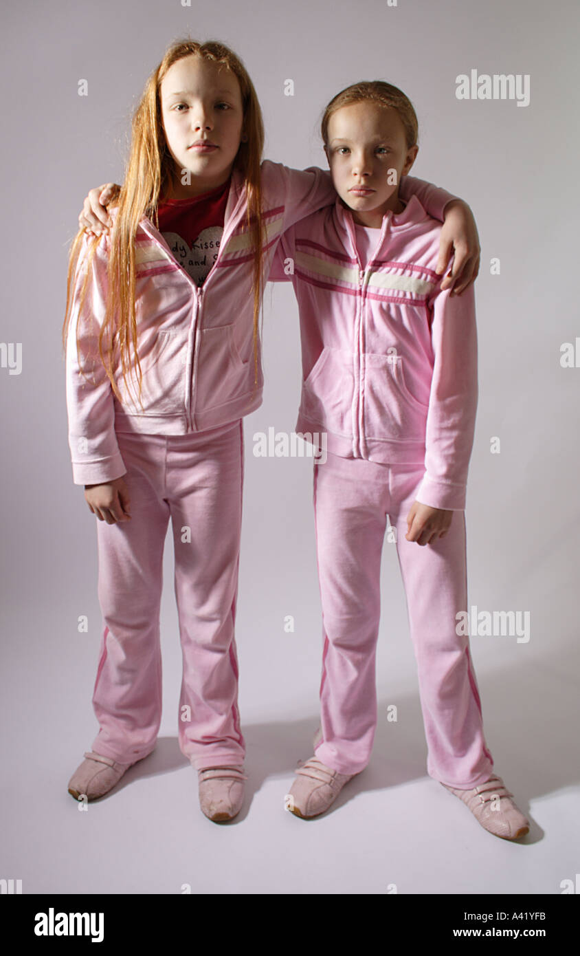 Young twin girls aged 10 standing upright looking apprehensively ...