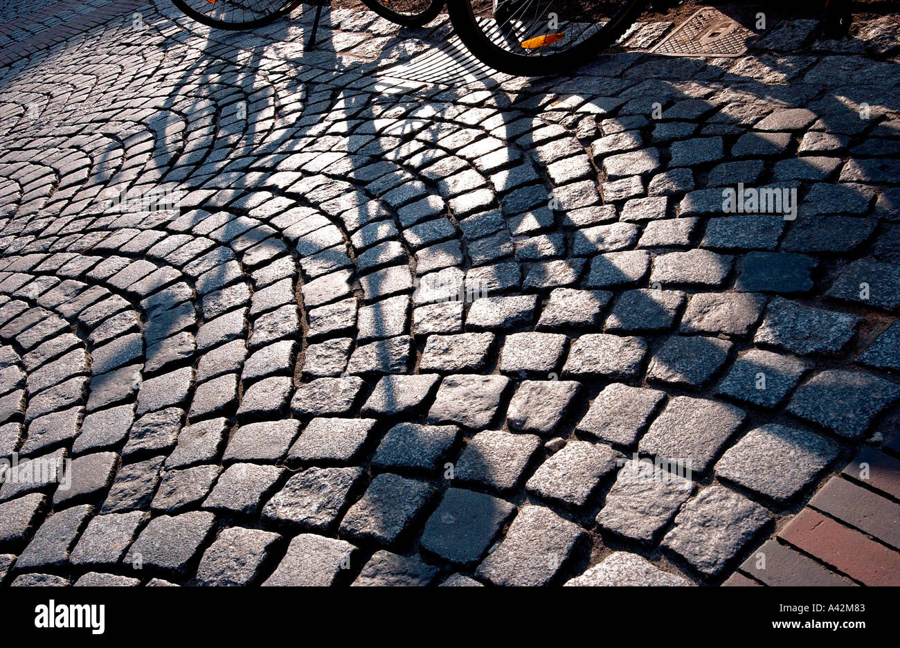 The shadow of a bicycle is cast on decorative cobble stones in a city ...