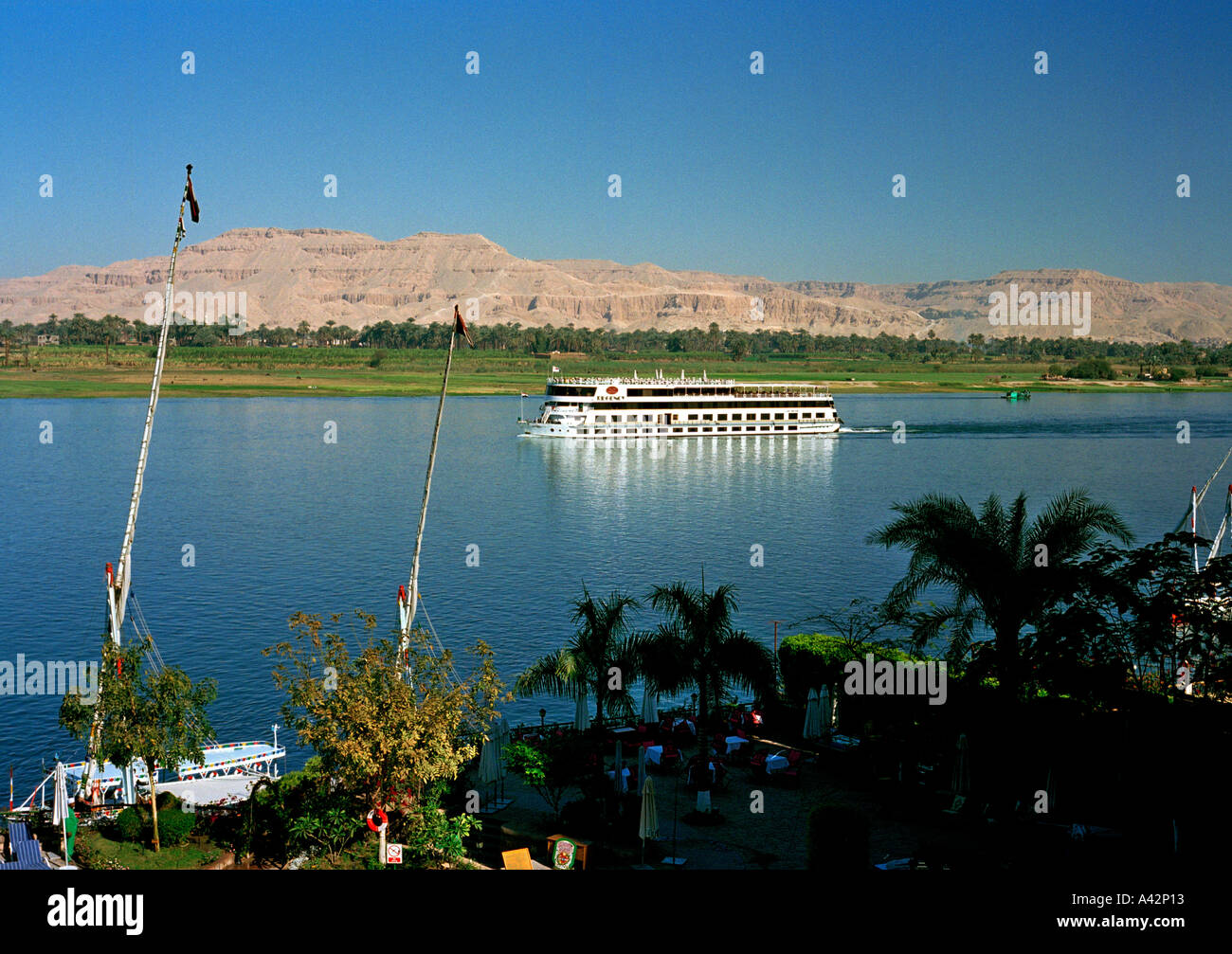 A Nile cruise boat heads to Aswan on a still morning with the desrt of ...
