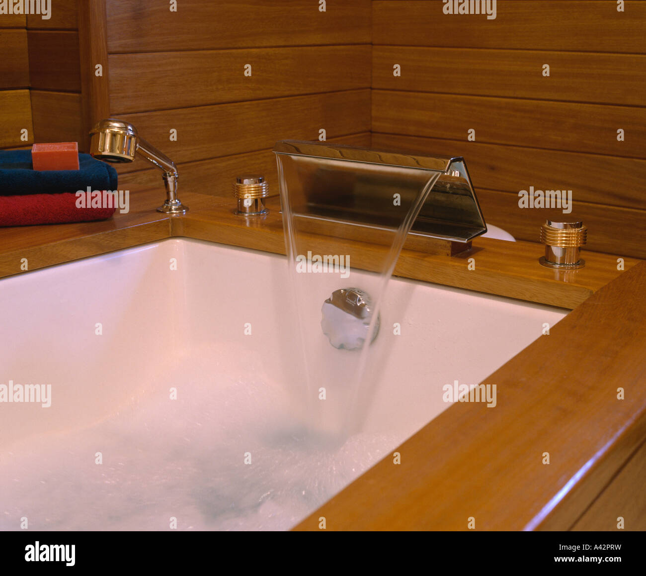 White bath with wooden surround and faucet on with water pouring into ...