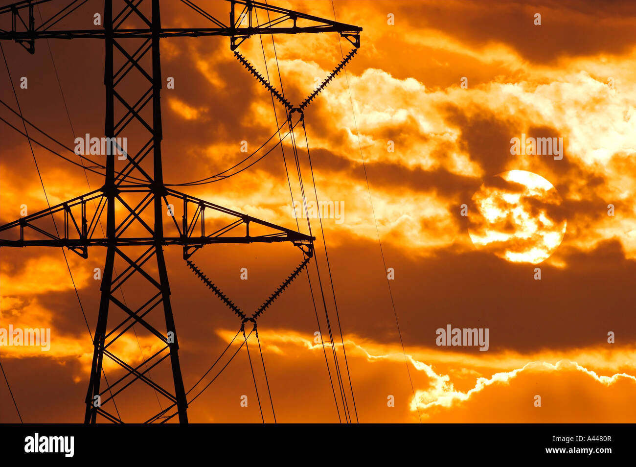 High tension power line tower at sunset with large sun disk partially ...