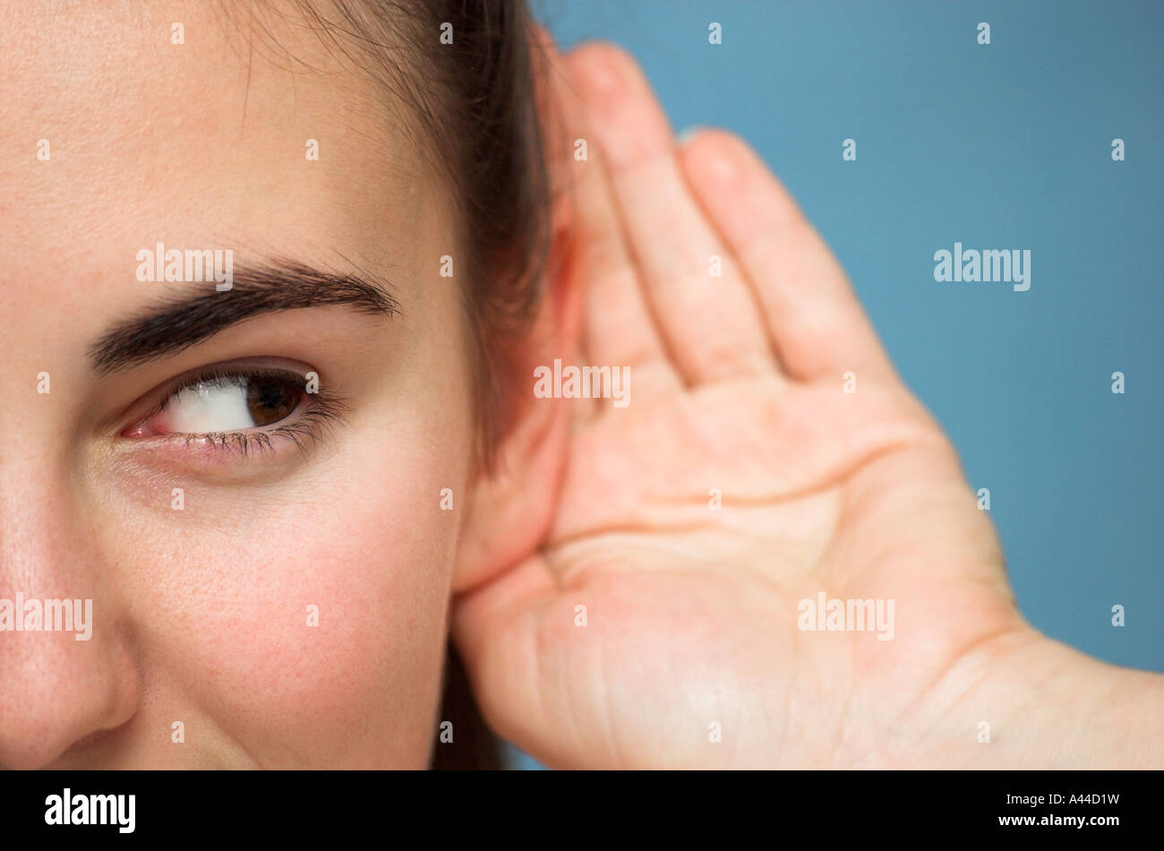 Young woman cupping hand to ear close up Stock Photo - Alamy