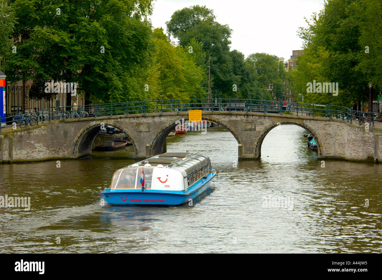 Wide canal excursion boat heading toward a low narrow bridge in ...