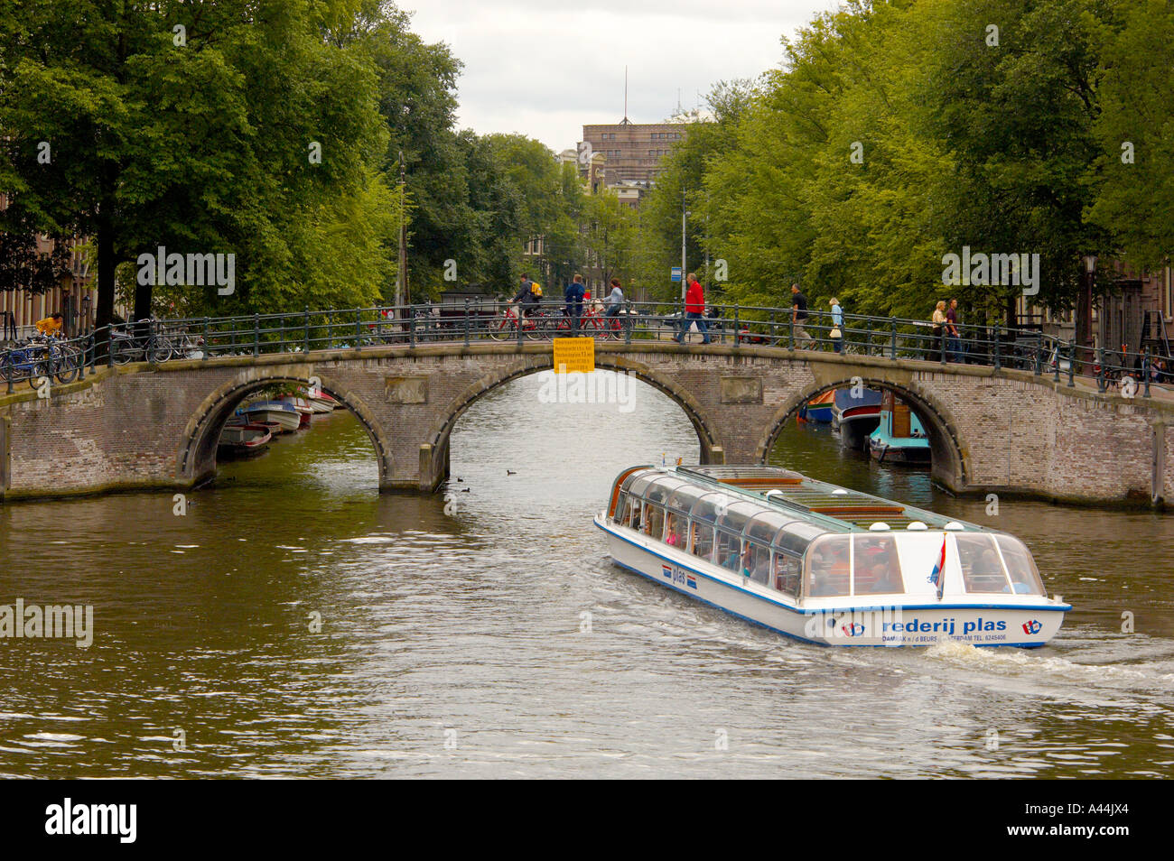 Wide canal excursion boat heading toward a low narrow bridge in ...