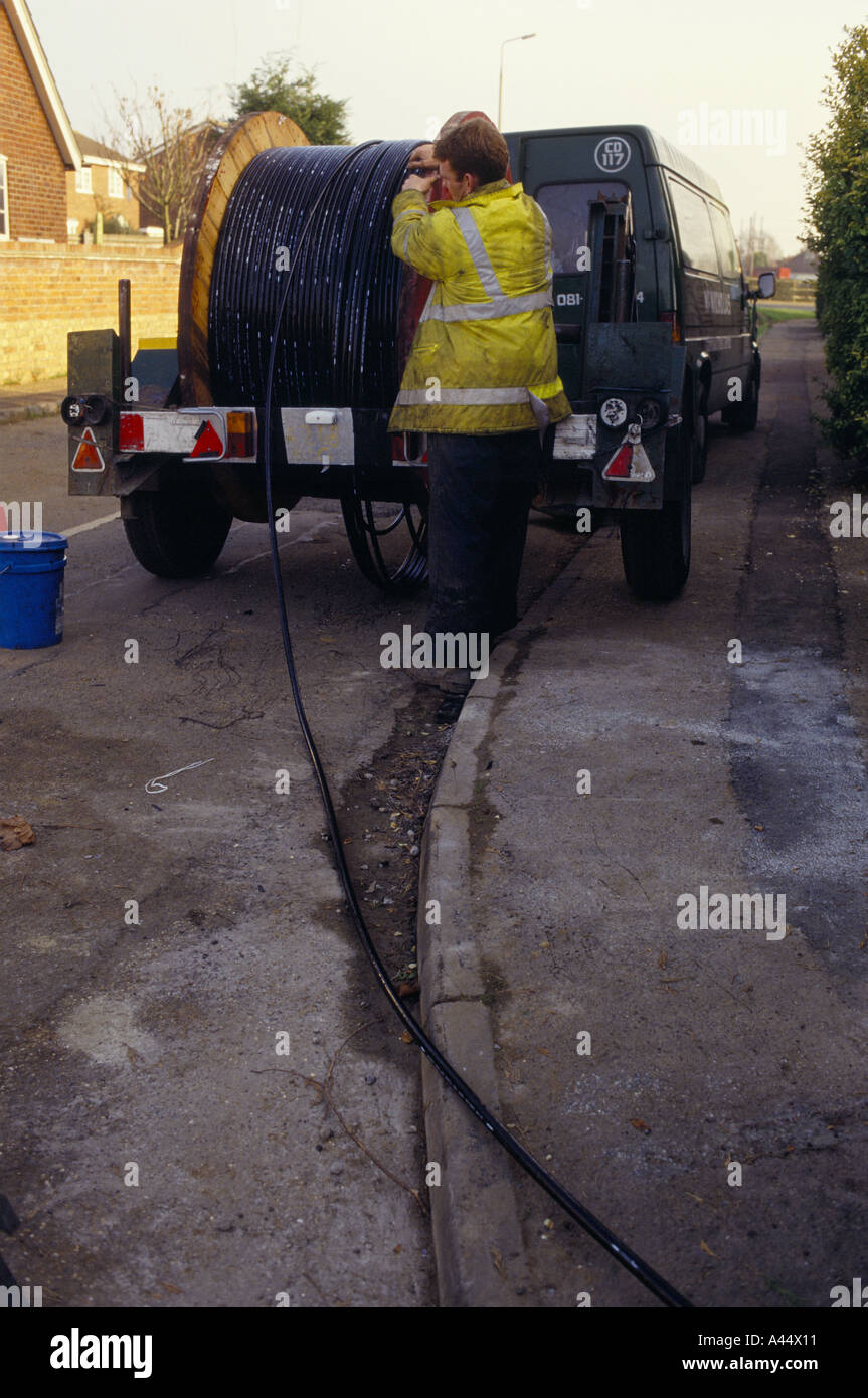 workman laying cable tv pipes from drum mounted on trailer for cable ...