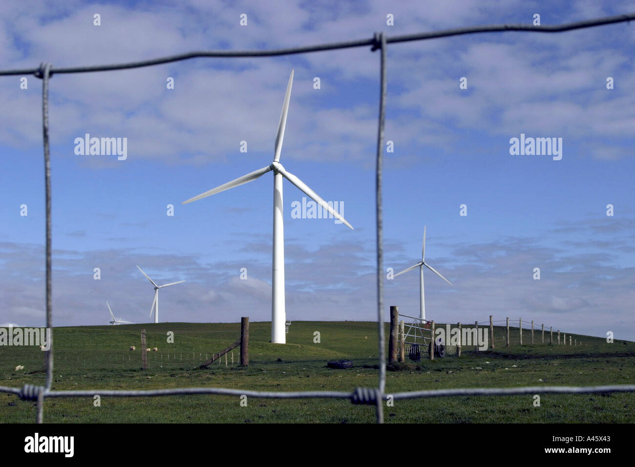 view through wire netting at windmill electricity turbines on the ...