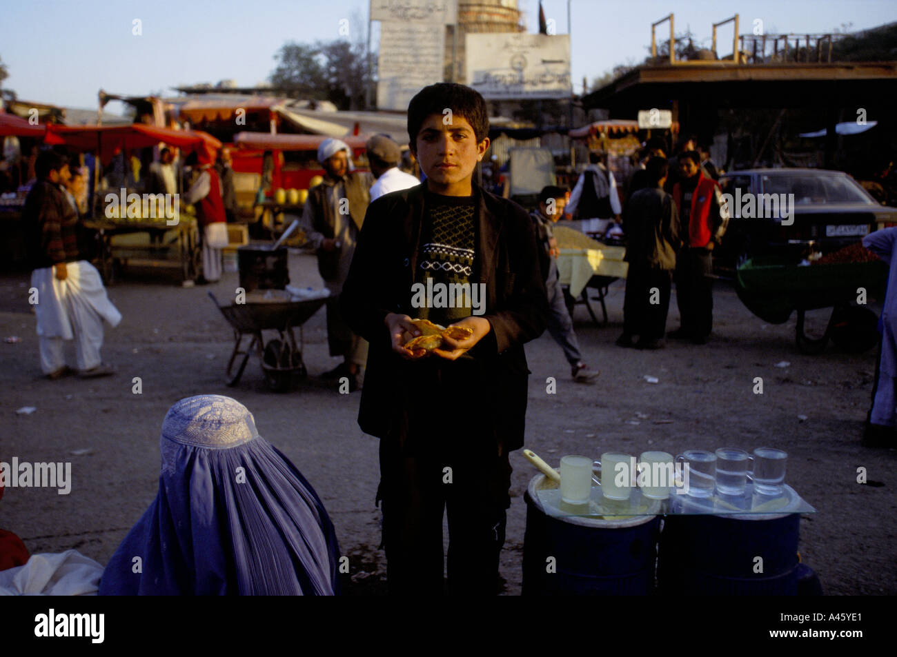 A boy sells food on the street with his mother at a market in Mazar i ...