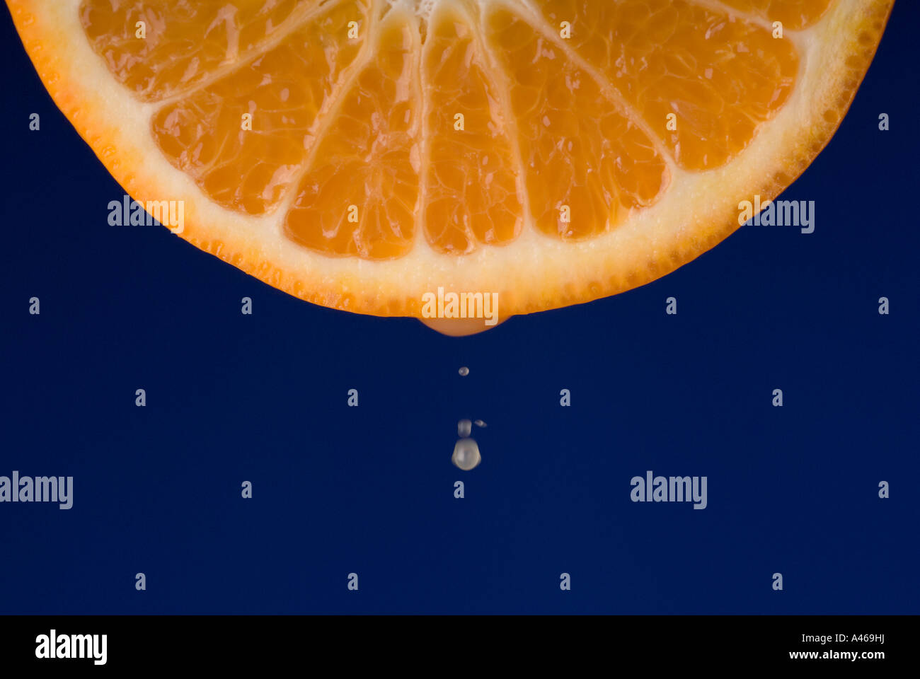 Drops of juice falling from freshly cut orange isolated on a blue ...