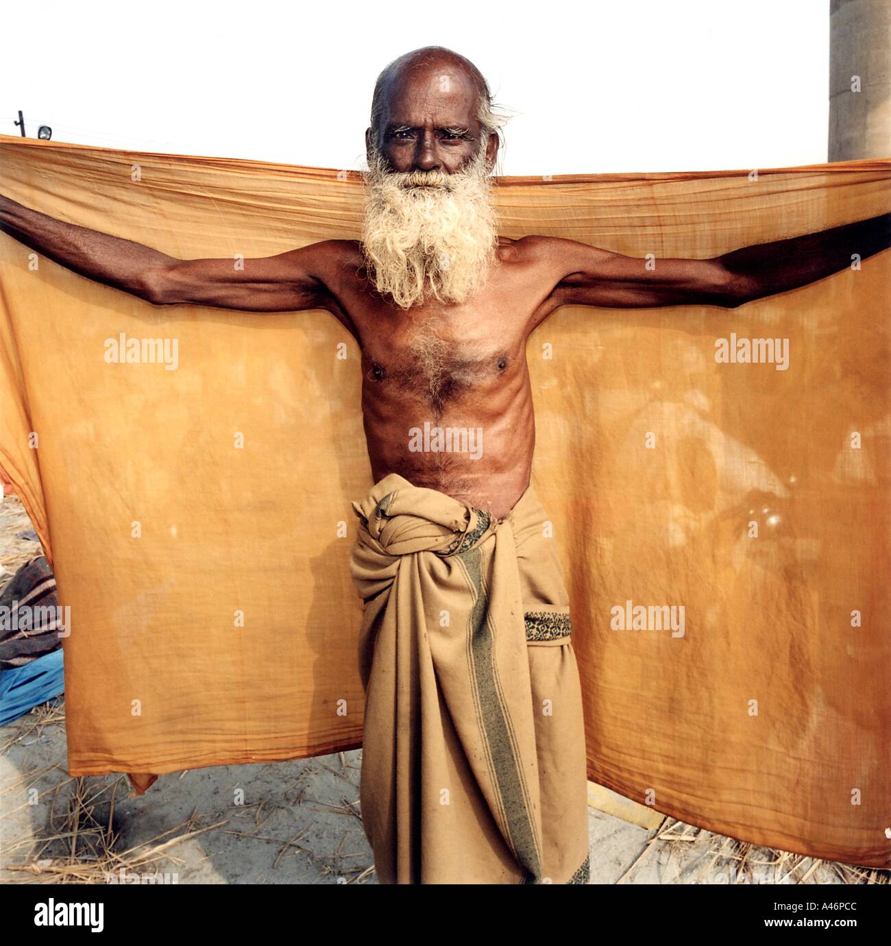 An elderly pilgrim dries his robe after bathing in the Ganges at the ...