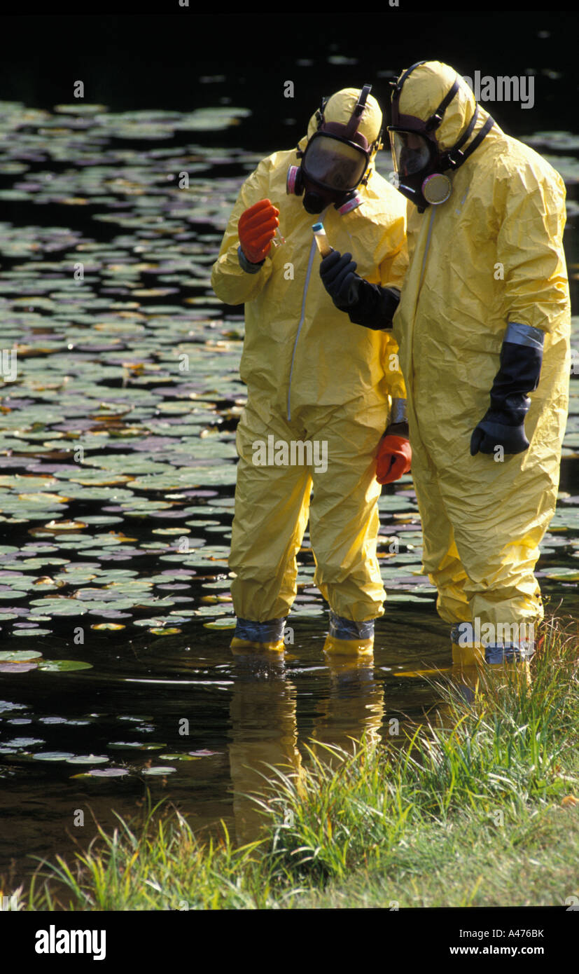 Two workers in protective suits test chemical levels in a body of water ...