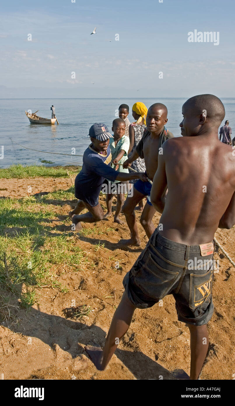 Fishermen and villagers hauling in nets onto shore of Lake Albert ...