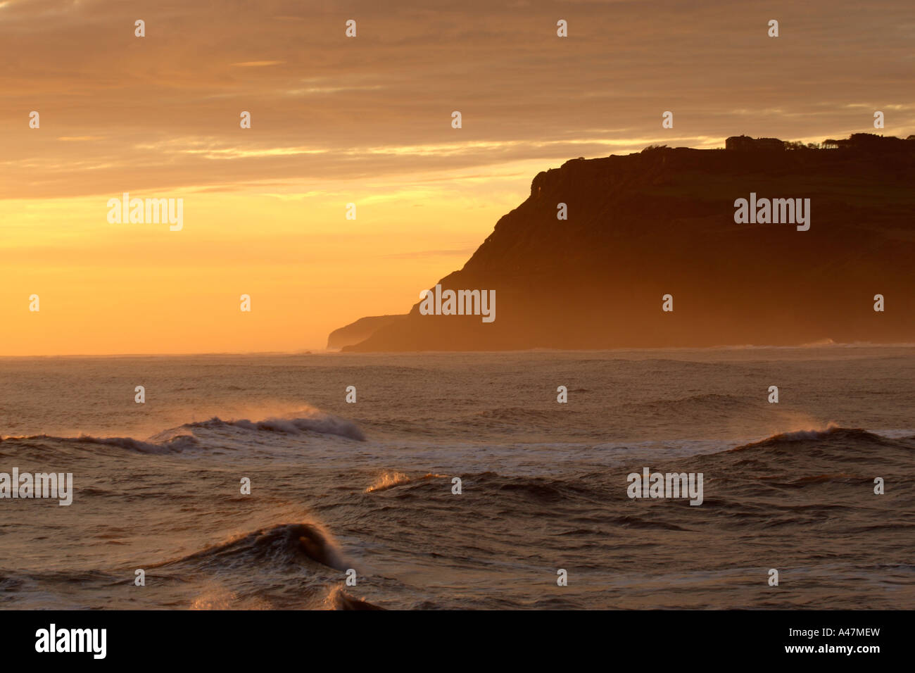 Cliffs at dawn dropping into an energetic sea lit by warm hues of a ...