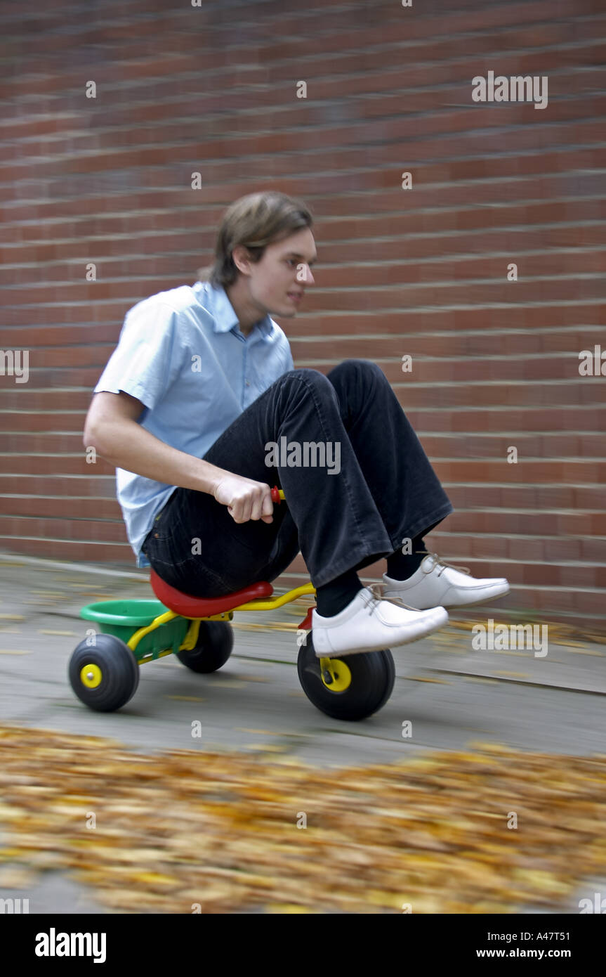 Young man riding small Childrens toy tricycle or bike Stock Photo - Alamy