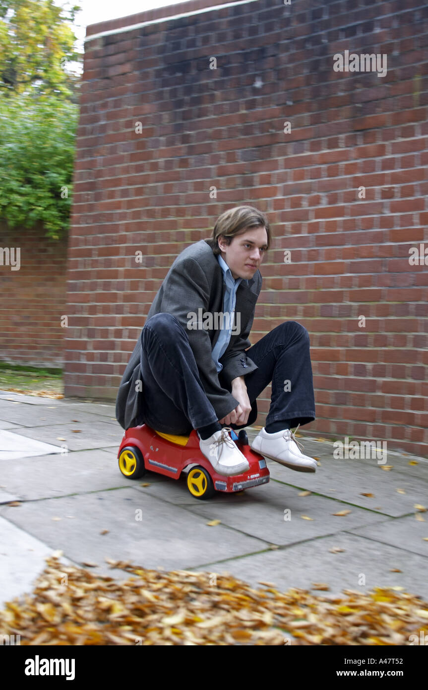 Young man riding small toy car Stock Photo - Alamy