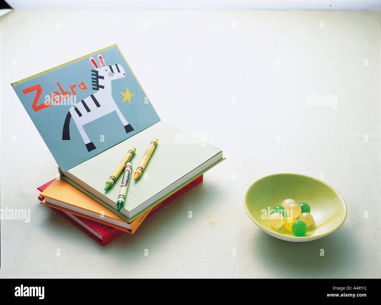 Crayons on a picture books with a bowl of candy Stock Photo - Alamy